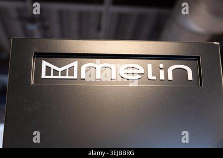 Close-up of Melin logo sign on dark display inside retail space ...