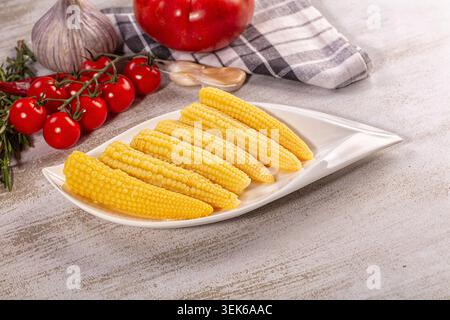 Baby corn arranged on white plate with cherry tomatoes garlic checkered ...