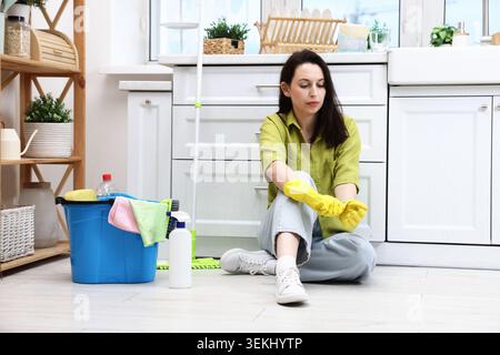 Tired woman with cleaning supplies sitting on floor in kitchen Stock ...