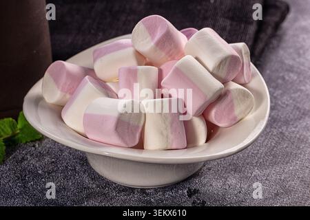 Pink white marshmallows piled in textured ceramic bowl with mint leaf ...