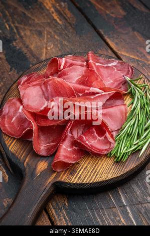 Thin slices of cured meat arranged on wooden board with fresh basil ...