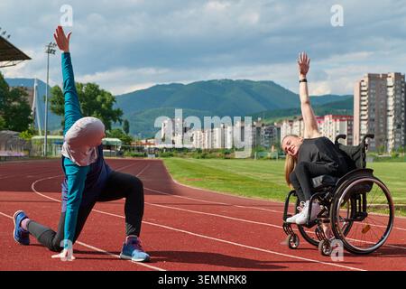 Female Wheelchair Athlete Stretching With Coach On Track At Empty ...