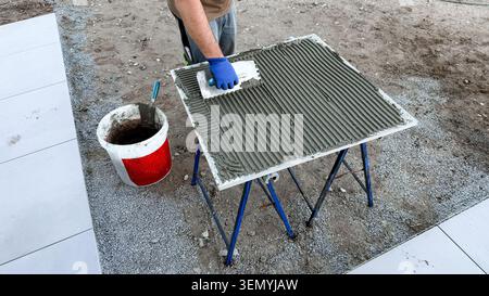 Construction worker applying adhesive mortar on a tile surface using a ...