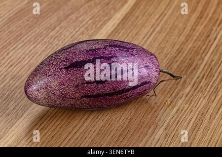 Single purple fruit with dark stripes speckled skin rests on textured ...