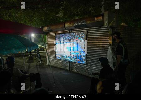 People watch a basketball game projected onto a screen in an outdoor ...