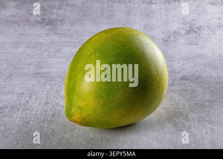 Fresh green pomelo with textured peel resting on rustic gray wood ...