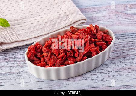 Vibrant red goji berries fill white square bowl on weathered wood table ...