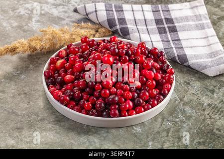 Vibrant red cranberries fill rustic wooden bowl on stone surface. Gray ...