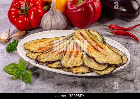 Grilled eggplant slices arranged on textured white plate with fresh ...