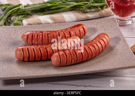Three sausages arranged on white plate with small bowl of ketchup ...