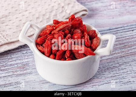 Vibrant red goji berries fill white square bowl on weathered wood table ...