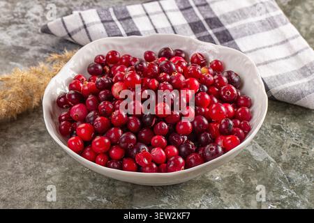 Vibrant red cranberries fill rustic wooden bowl on stone surface. Gray ...