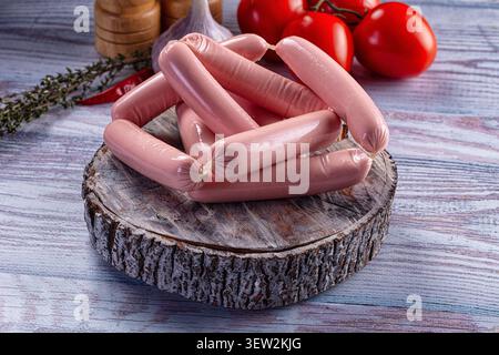 Raw pink sausages arranged on rustic wooden board with fresh red ...