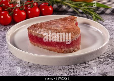 Seared tuna steak with pink center on white plate. Cherry tomatoes ...