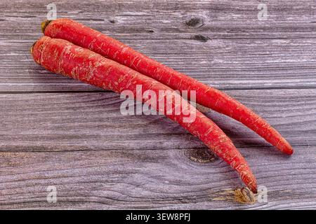 Two unpeeled orange carrots rest diagonally on weathered wood surface ...