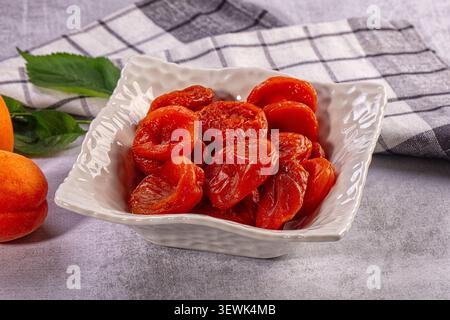 Vibrant orange dried apricots fill scalloped ceramic bowl on weathered ...