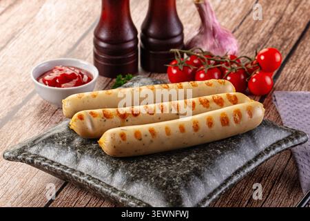 Three sausages arranged on white plate with small bowl of ketchup ...