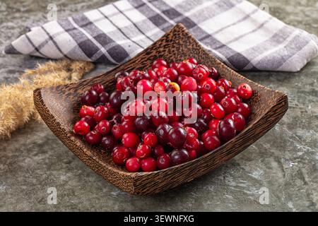 Vibrant red cranberries fill rustic wooden bowl on stone surface. Gray ...