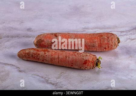 Two unpeeled orange carrots rest diagonally on weathered wood surface ...