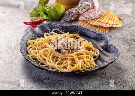 Spaghetti with mussels served on textured white plate. Warm golden ...