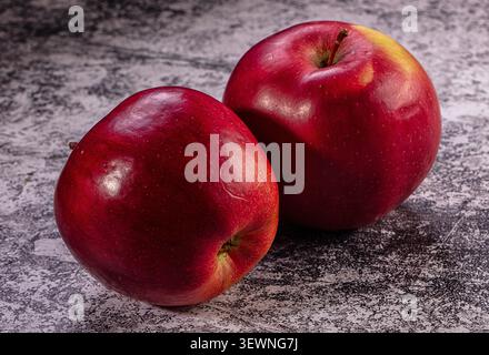 Two shiny red apples rest on weathered wood surface. Warm lighting ...
