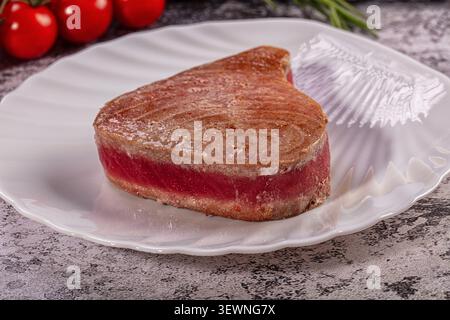 Seared tuna steak with pink center on white plate. Cherry tomatoes ...