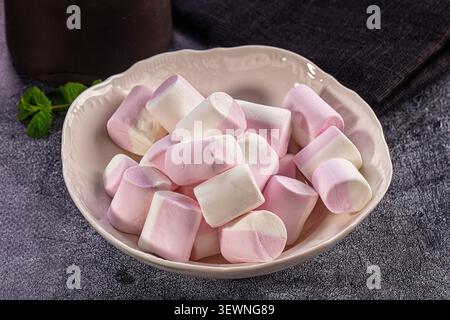 Pink white marshmallows piled in textured ceramic bowl with mint leaf ...