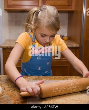 A girl is using the rolling pin to roll out the dough on the table ...