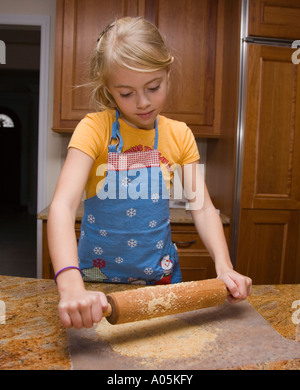 A girl is using the rolling pin to roll out the dough on the table ...