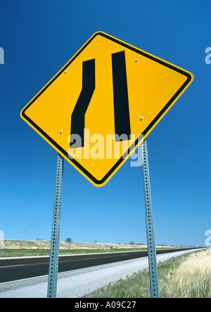 A yellow and black diamond shaped merge left road sign on a thick ...