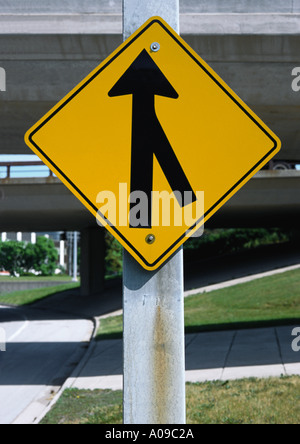A yellow and black diamond shaped merge left road sign on a thick ...