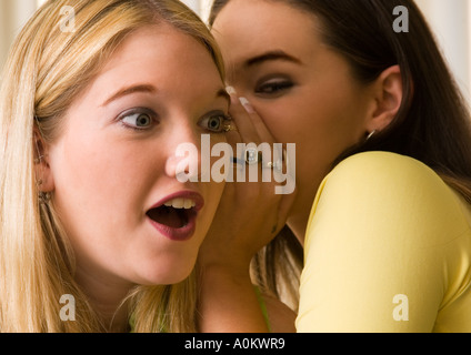 White girl whispering secret to her shocked friend isolated over yellow ...