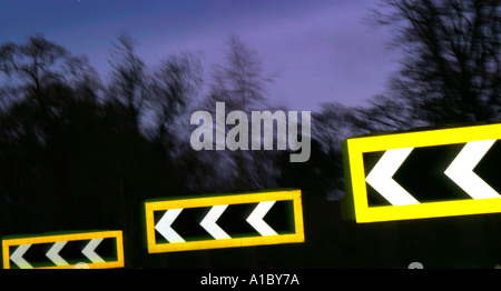 Chevron road sign indicating a left hand corner, cut into a conifer ...