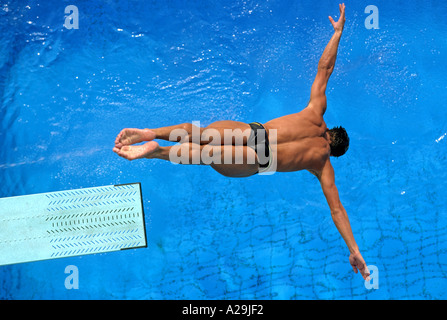 Overhead view of a male springboard diver plunging into the pool during ...