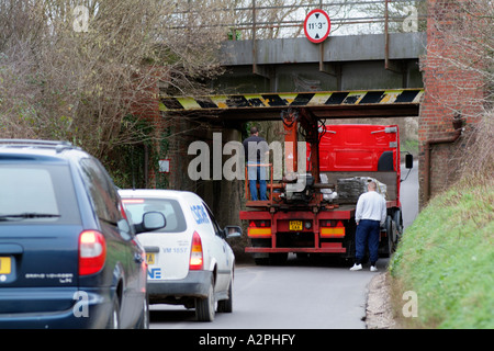 An articulated lorry stuck under a low bridge on an English country ...