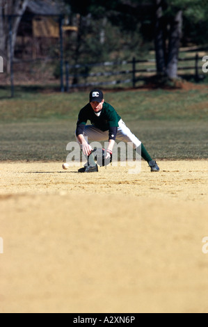 A high school baseball player fielding the ball on red turf field ...