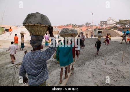 Workers carrying heavy baskets of sand on their heads from the boat to ...