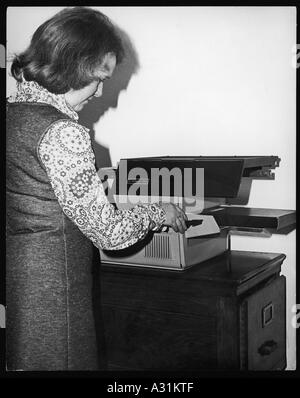 A woman in a floral shirt and with a "page boy" hairstyle, using an ...