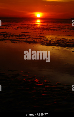 A fiery red sun drops toward the horizon in an intense sunset at dusk ...