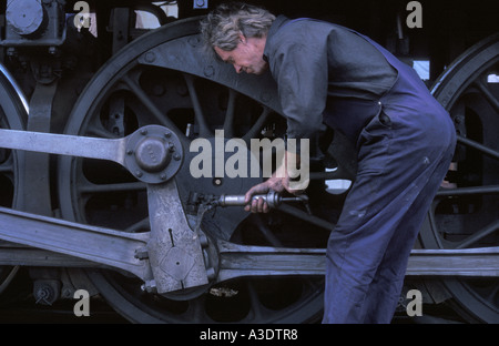 A train engineer in blue overalls crouching down and applying motor oil ...