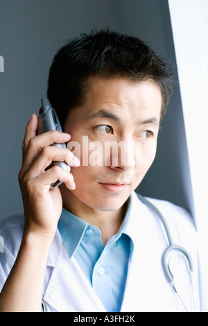 Asian doctor speaking on mobile phone at home discussing telehealth ...