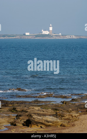 Deserted rocky beach at Amble with Coquet island lighthouse sitting on ...