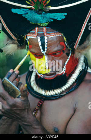 A Huli wigman using a hand mirror to put on traditional face paint Tari ...