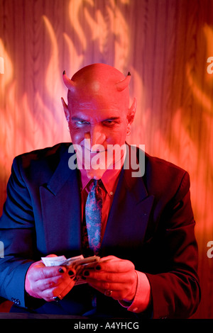 Businessman dressed as devil holding money Stock Photo - Alamy