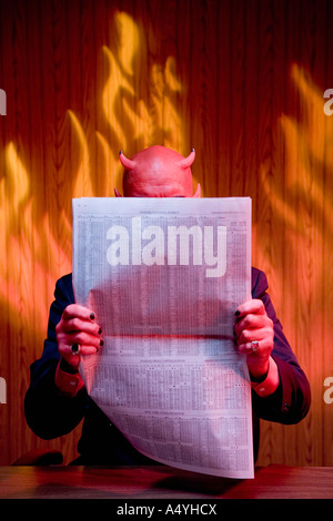 Businessman dressed as devil reading newspaper Stock Photo - Alamy