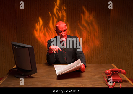Businessman dressed as devil reading newspaper Stock Photo - Alamy