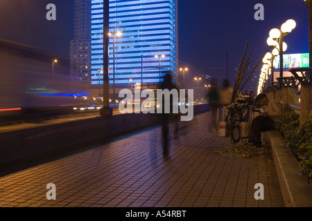 Sugar cane vendor with passing traffic and lit up building on a bridge ...