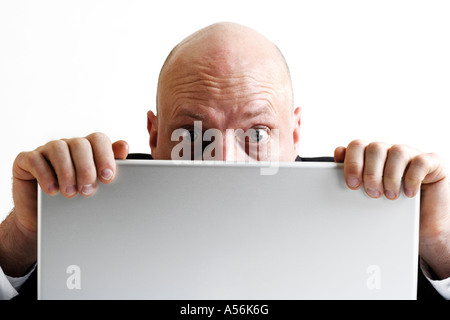 Surprised man with wide eyes hiding behind a laptop computer staring at ...