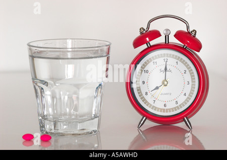 Alarm clock with pills and glass of water on shelf in room Stock Photo ...