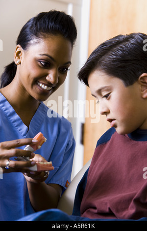 Dental hygienist holding false teeth talking to boy Stock Photo - Alamy